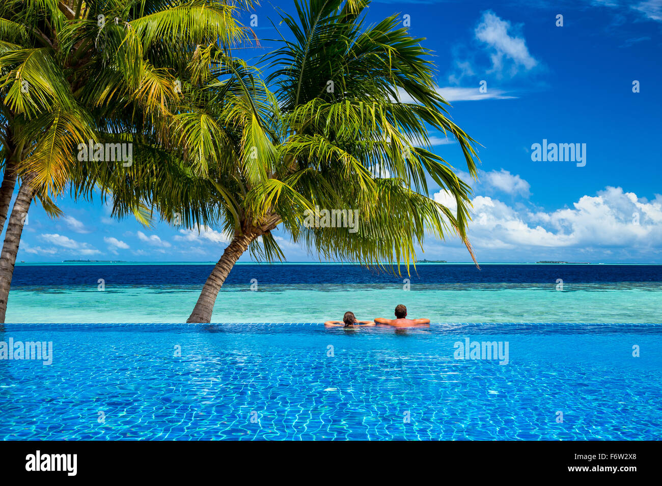 young couple relaxing in infinity pool under coco palms in front of ...