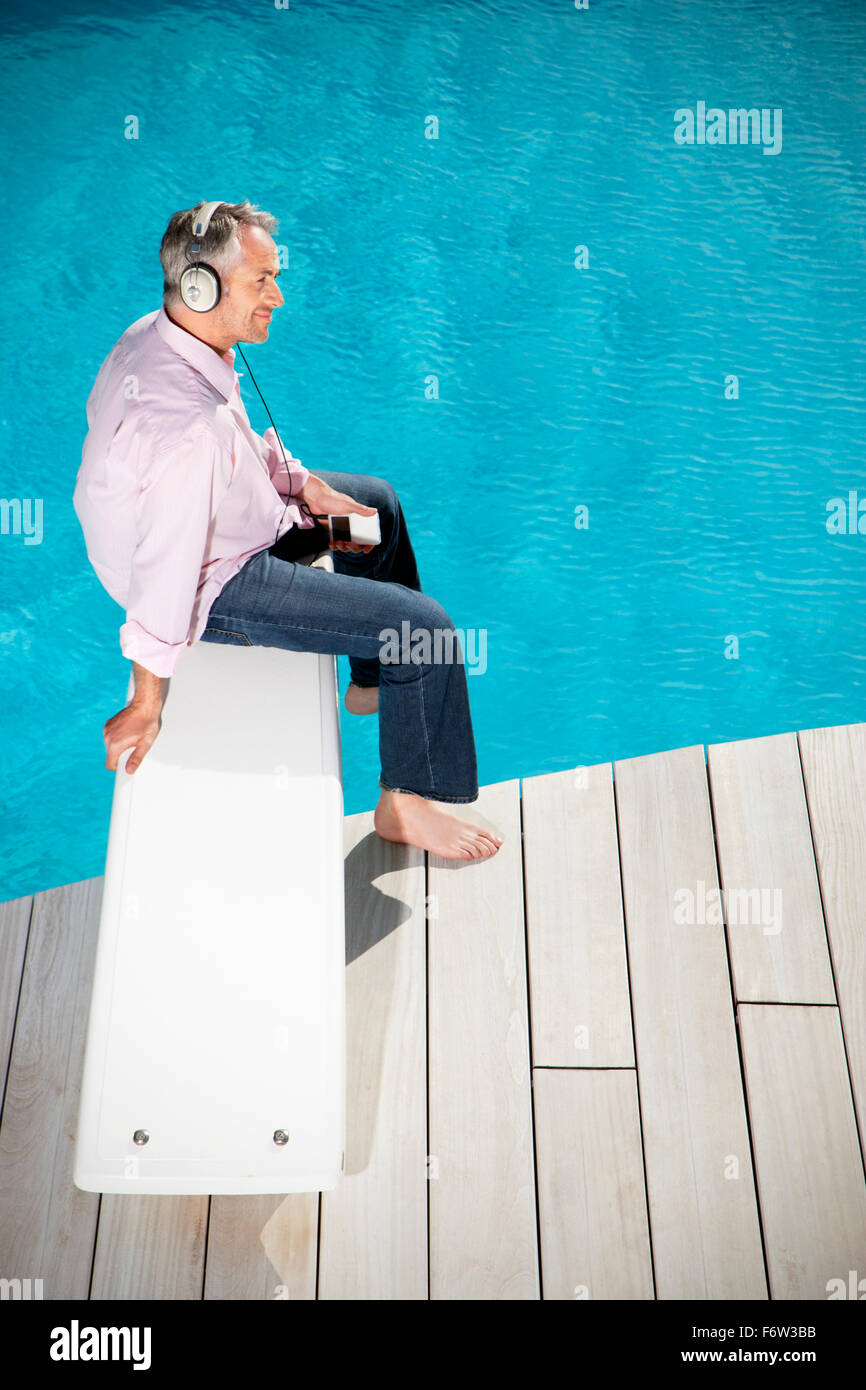 Spain, Mallorca, man sitting on springboard of a pool listening music ...