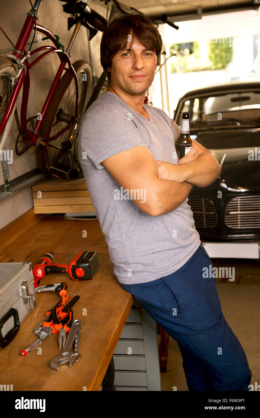 Smiling man in garage with bottle of beer and vintage car Stock Photo ...