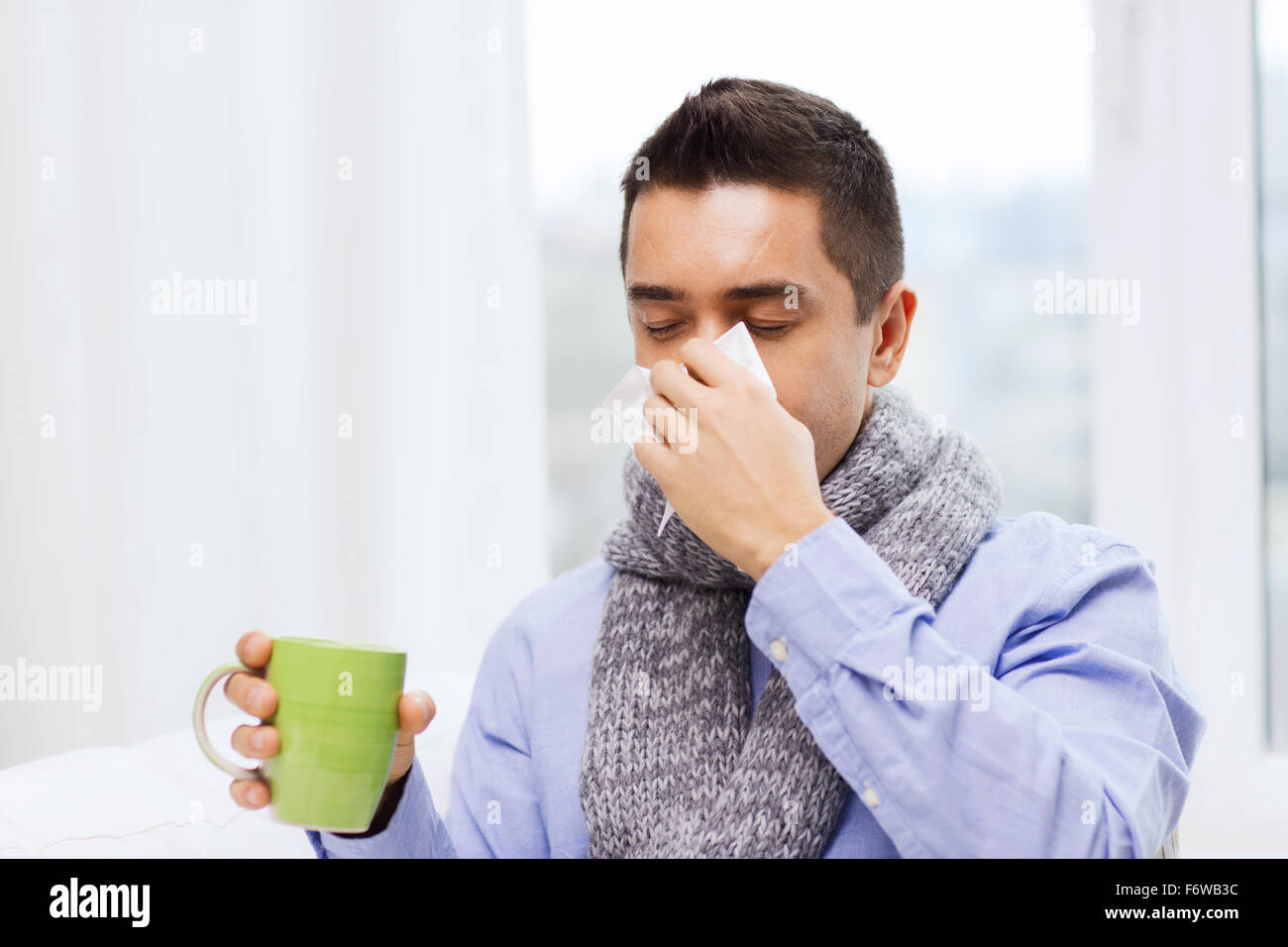 ill man with flu drinking tea and blowing nose Stock Photo - Alamy