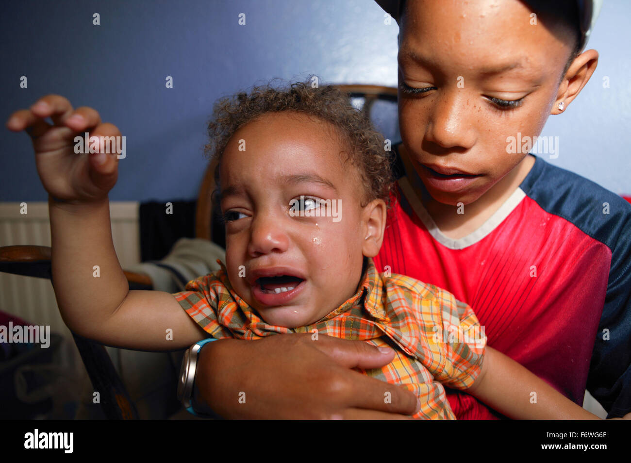 Young boy minding his crying baby brother Stock Photo - Alamy