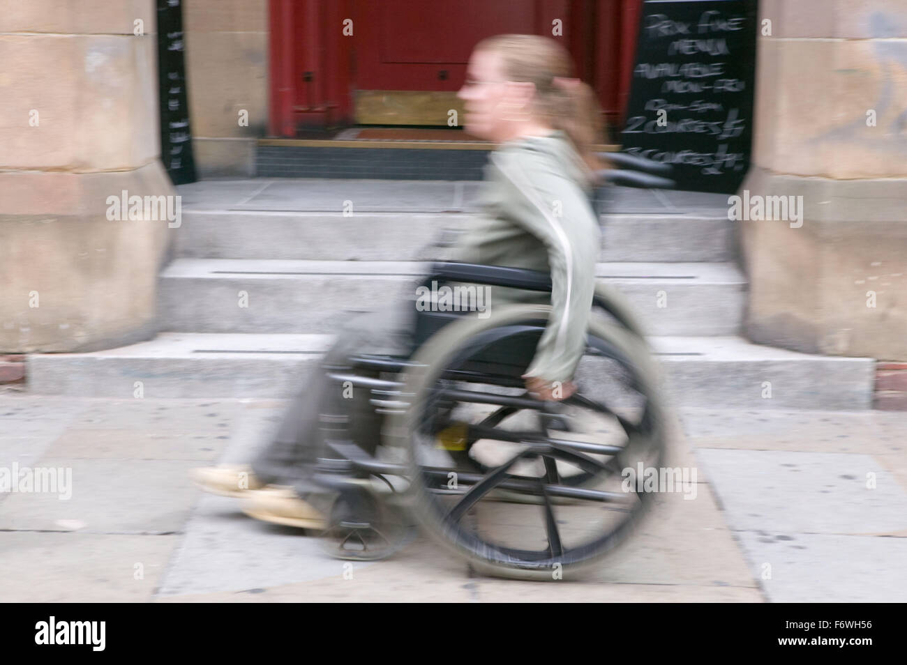 Young wheelchair user moving past a flight of steps which she is unable ...
