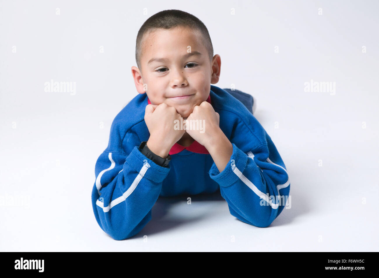 Young boy resting his head in his hands and lying on his front smiling ...