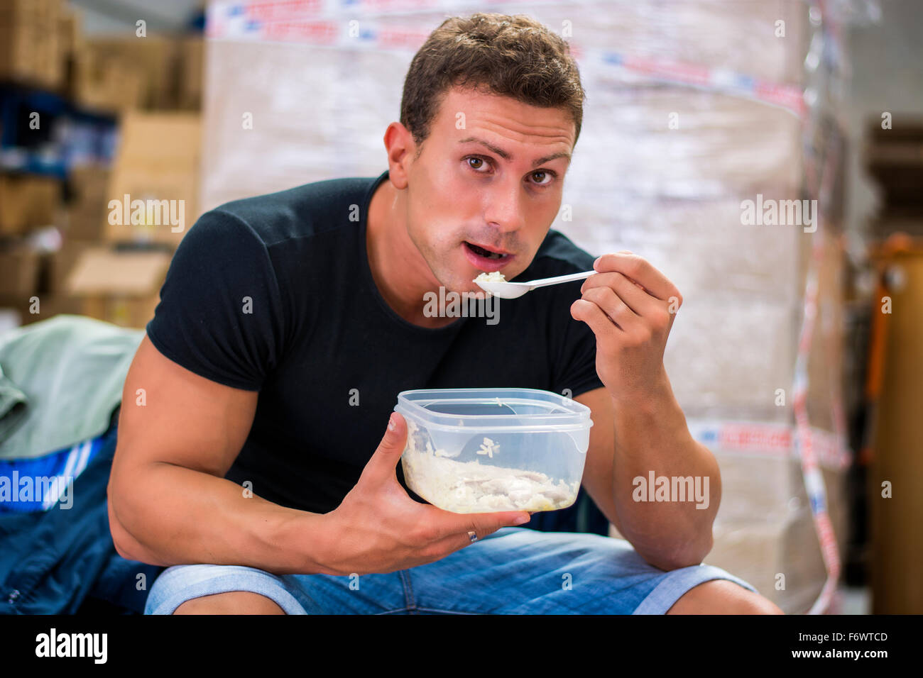 Hungry shirtless muscular young man gulping down food glancing across ...