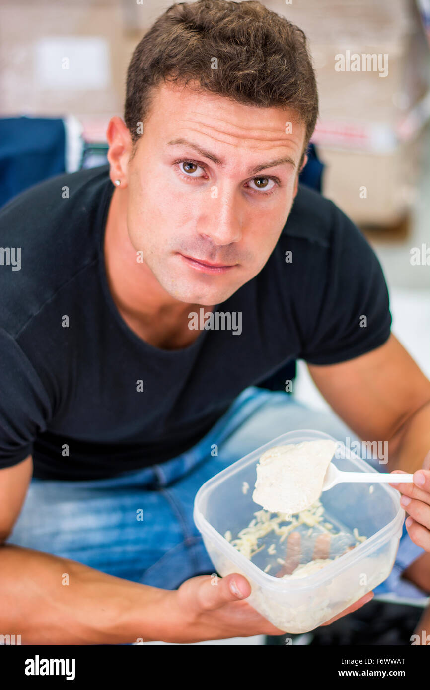 Hungry shirtless muscular young man gulping down food glancing across ...