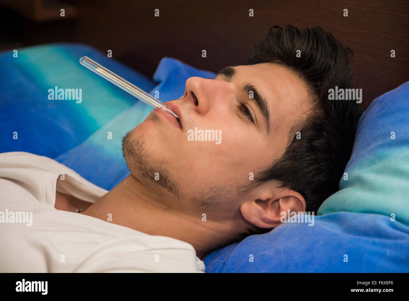 Young handsome man in bed with a flu or measuring fever with ...