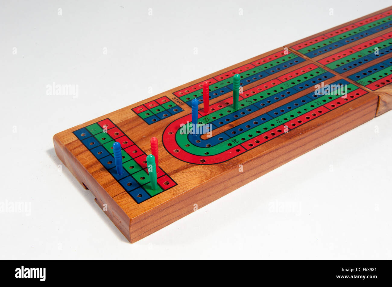 Cribbage board with red, green and blue pegs against a white background ...