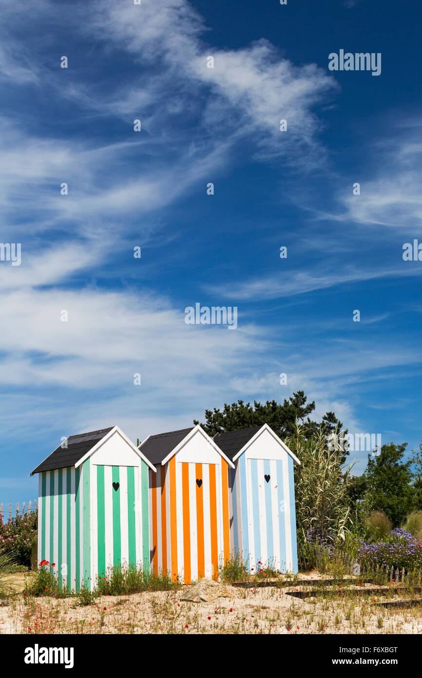 Three colourful striped painted outhouses on a sandy grassy hill with ...
