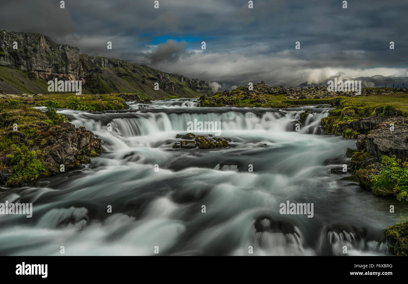 Water flowing over a rugged landscape under a cloudy sky; Iceland Stock ...