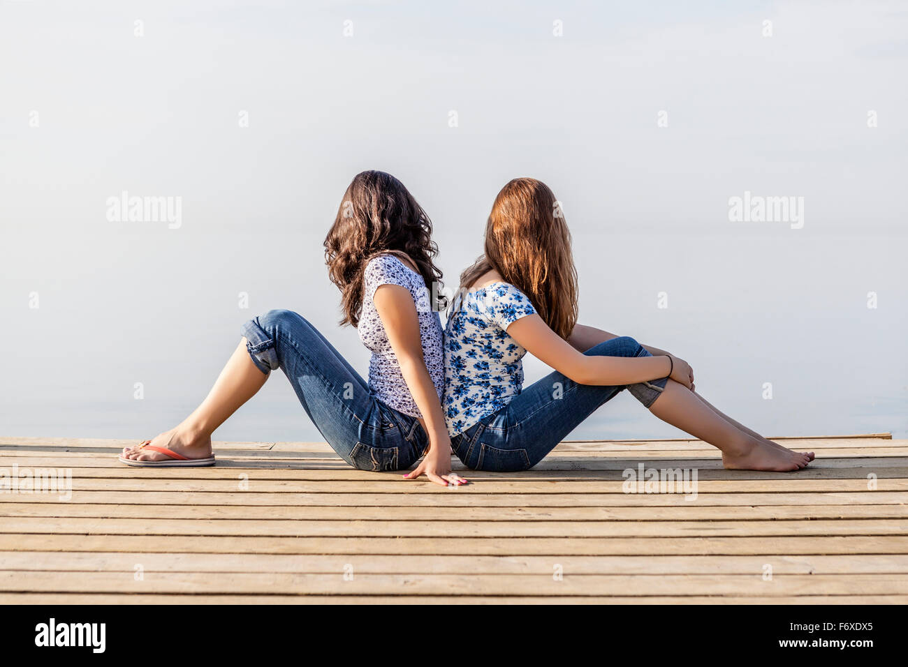 Two girls sitting back-to-back at end of a dock; Toronto, Ontario ...