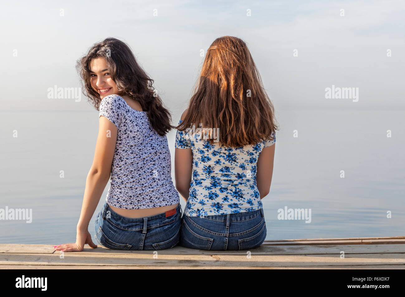 Two girls sitting close together at end of a dock; Toronto, Ontario ...