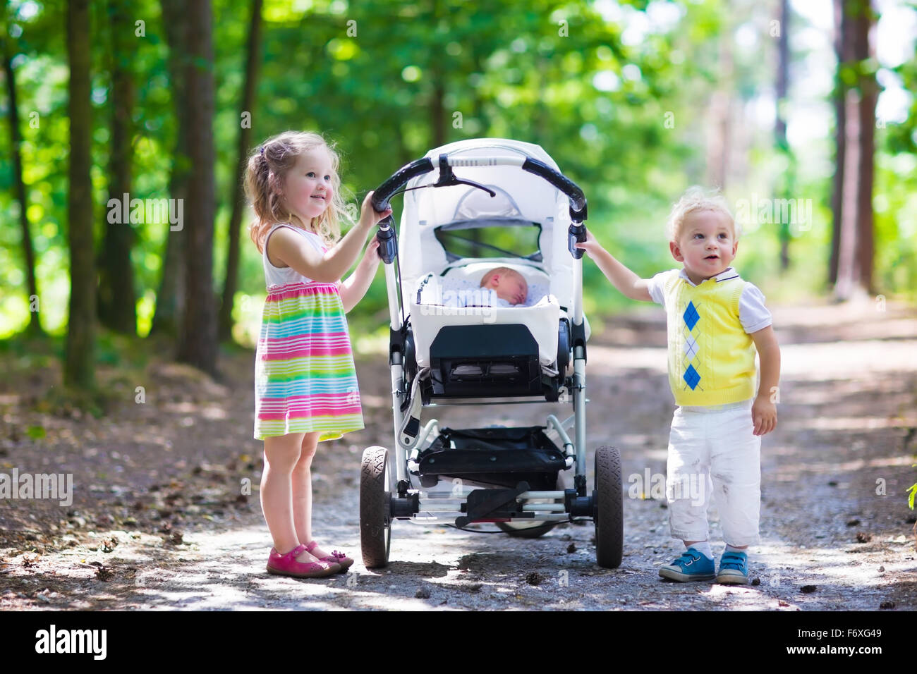 Boy and girl walk in sunny summer park pushing stroller with newborn ...