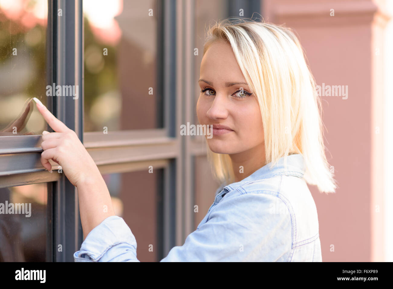 Pretty blond woman pointing to a glass windowpane in a window with her ...