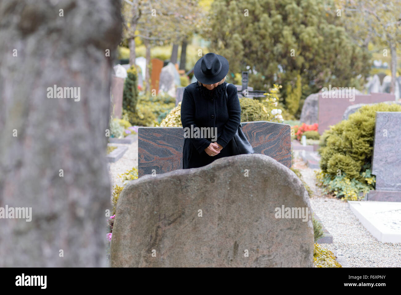 Woman in mourning dressed in full black praying at a graveside standing ...