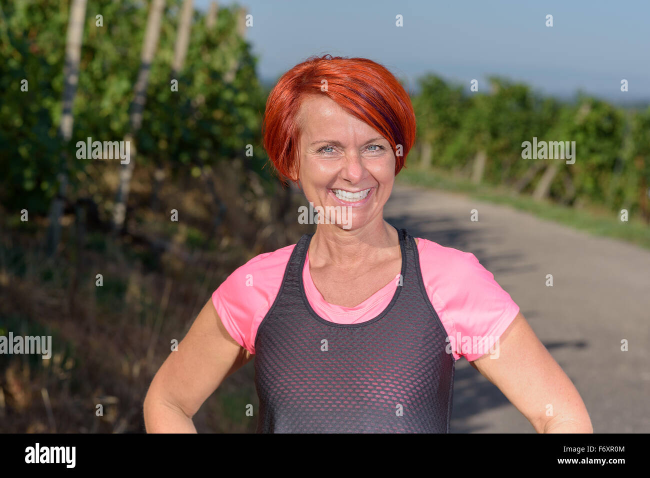 Healthy vivacious pretty redhead woman out for her evening jog standing ...