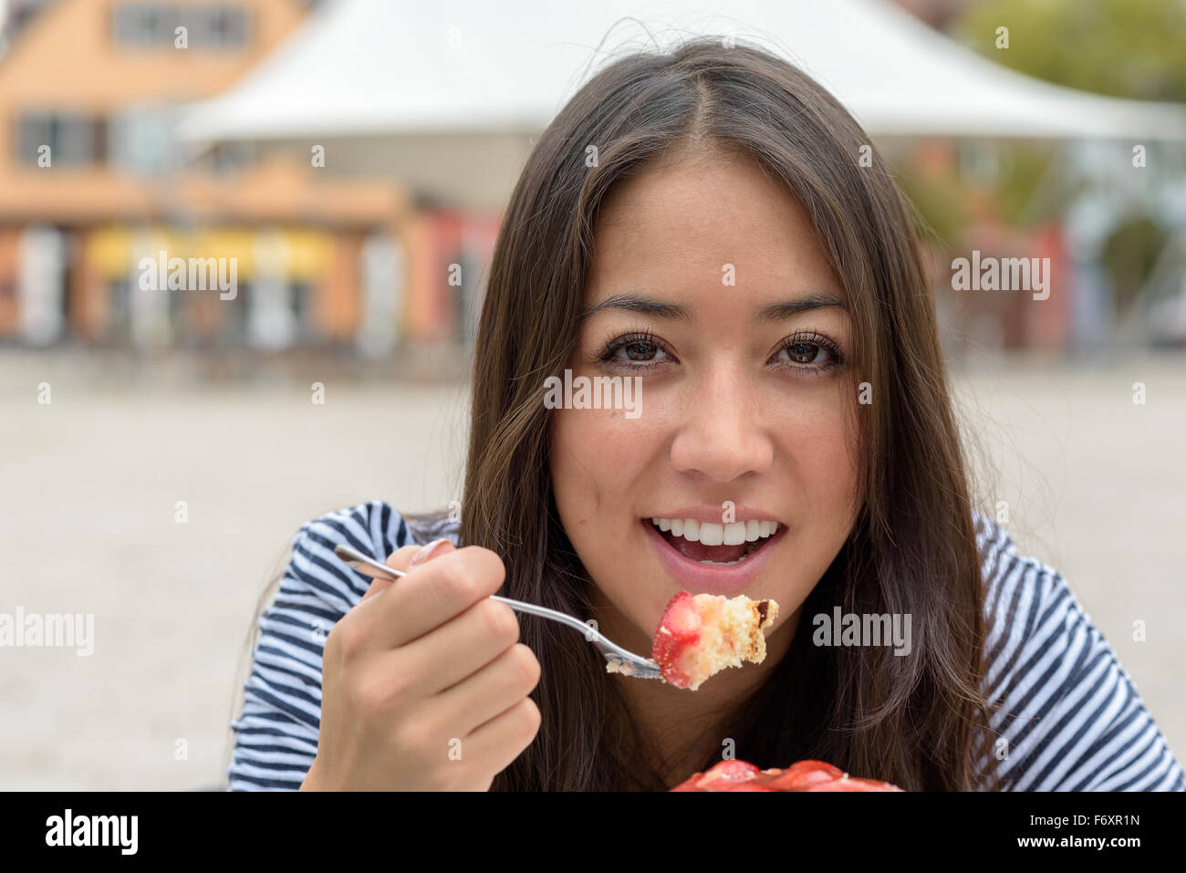 Happy woman enjoying eating a cake for dessert as she sits at a table ...