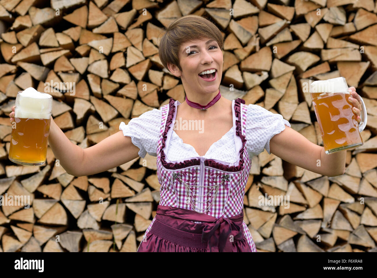 Vivacious woman in a dirndl holding two beers in glass tankards in her ...