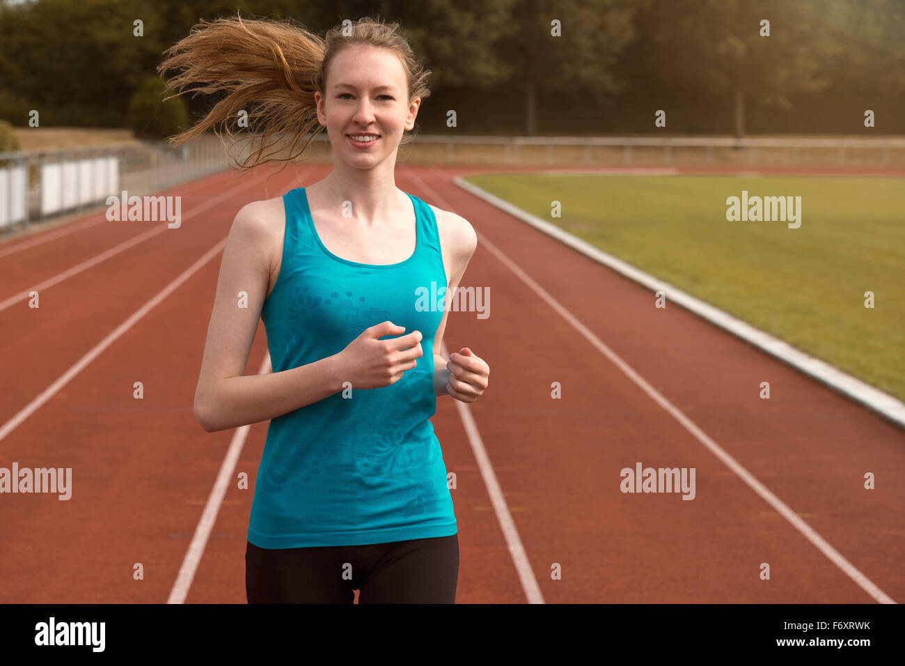 Young woman runner training on a race track approaching the camera with ...