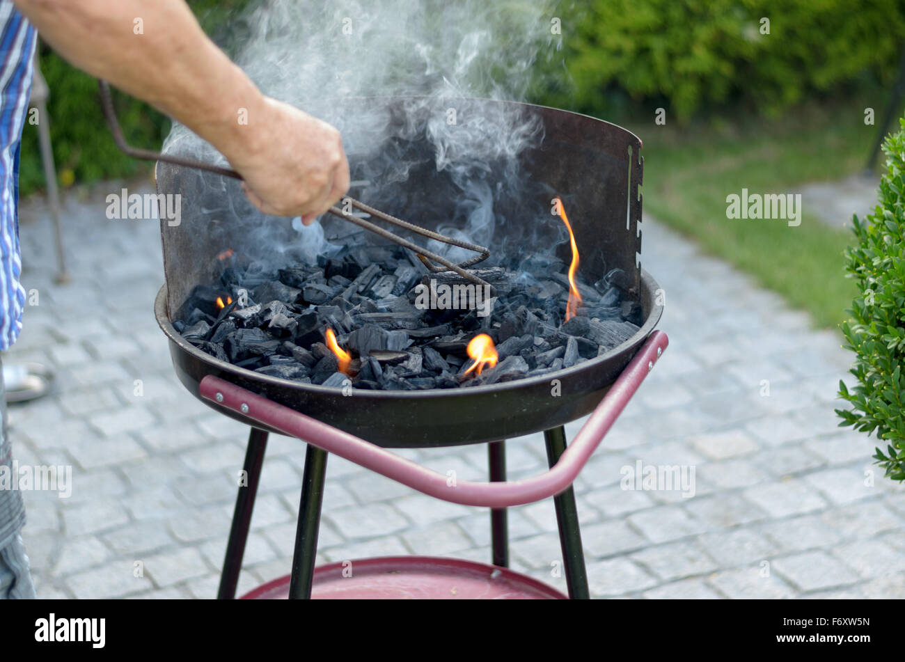 Man standing outdoors on a green lawn cooking meat on a portable ...