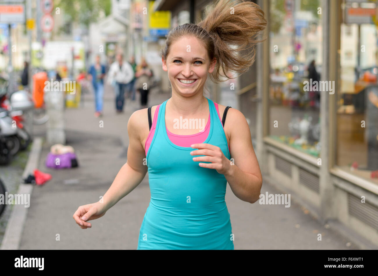 Happy energetic young woman jogging through town with her ponytail ...