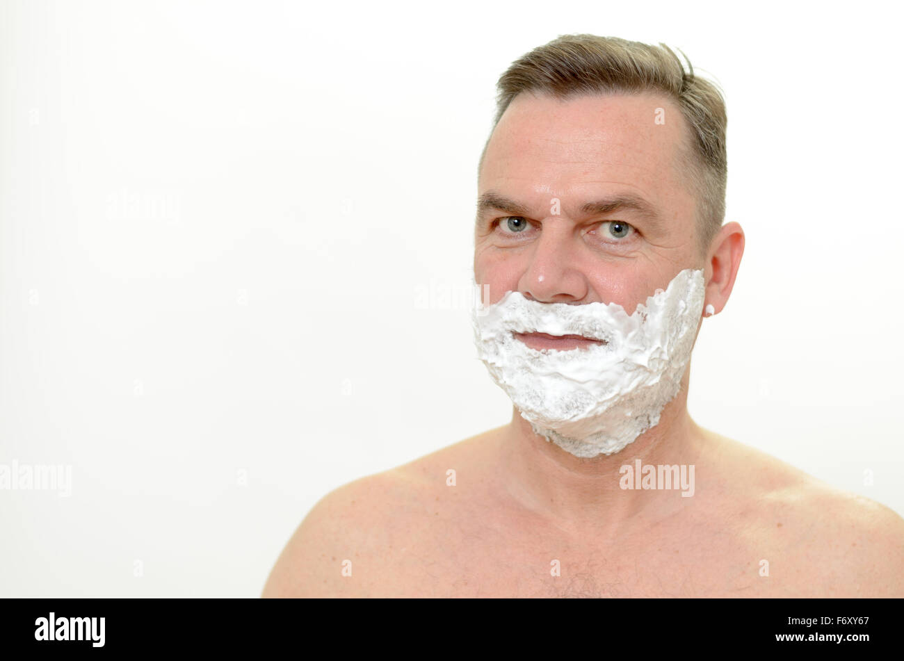 Man preparing to shave his beard standing with lathered white shaving cream covering his lower ...