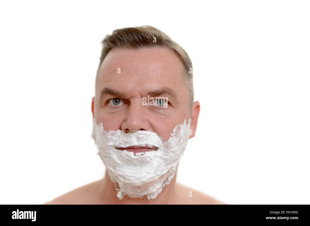 Man preparing to shave his beard standing with lathered white shaving cream covering his lower ...