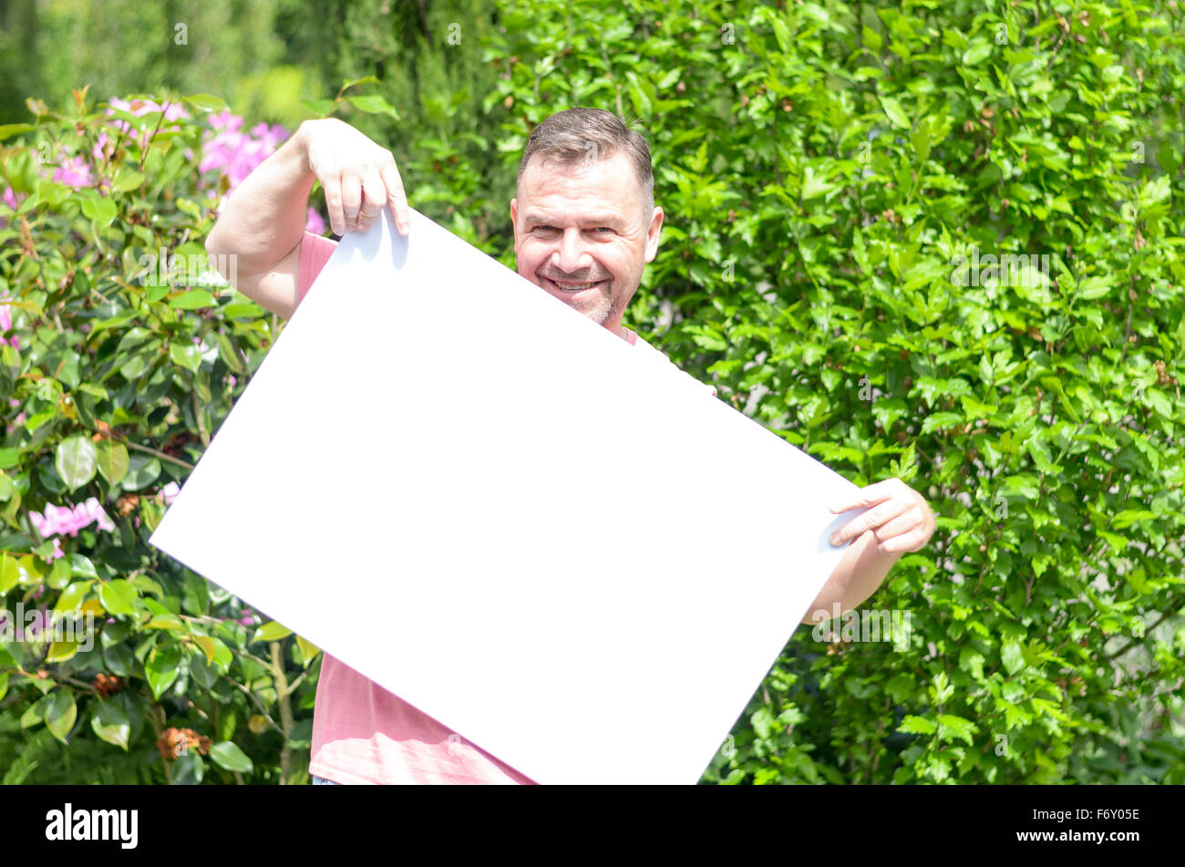 Young cheerful man smiling while holding and showing a blank whiteboard ...