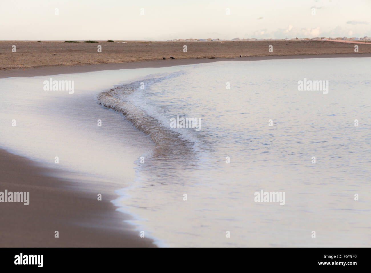 Waves from the ocean roll in, leaving the soft sandy beach damp ...