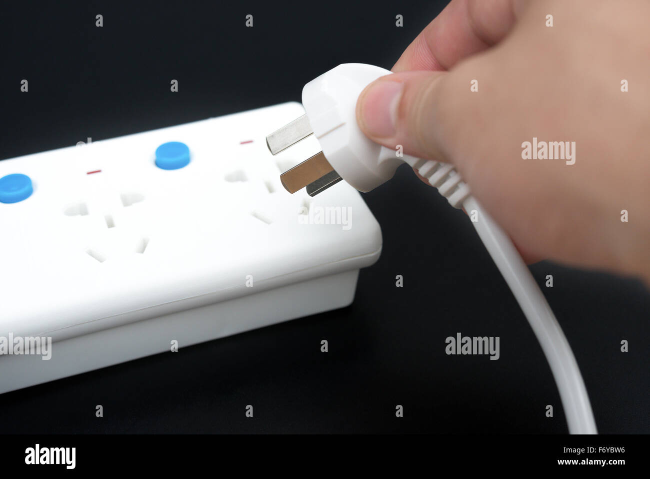 putting a plug to a multi sockets power extension on black Stock Photo ...