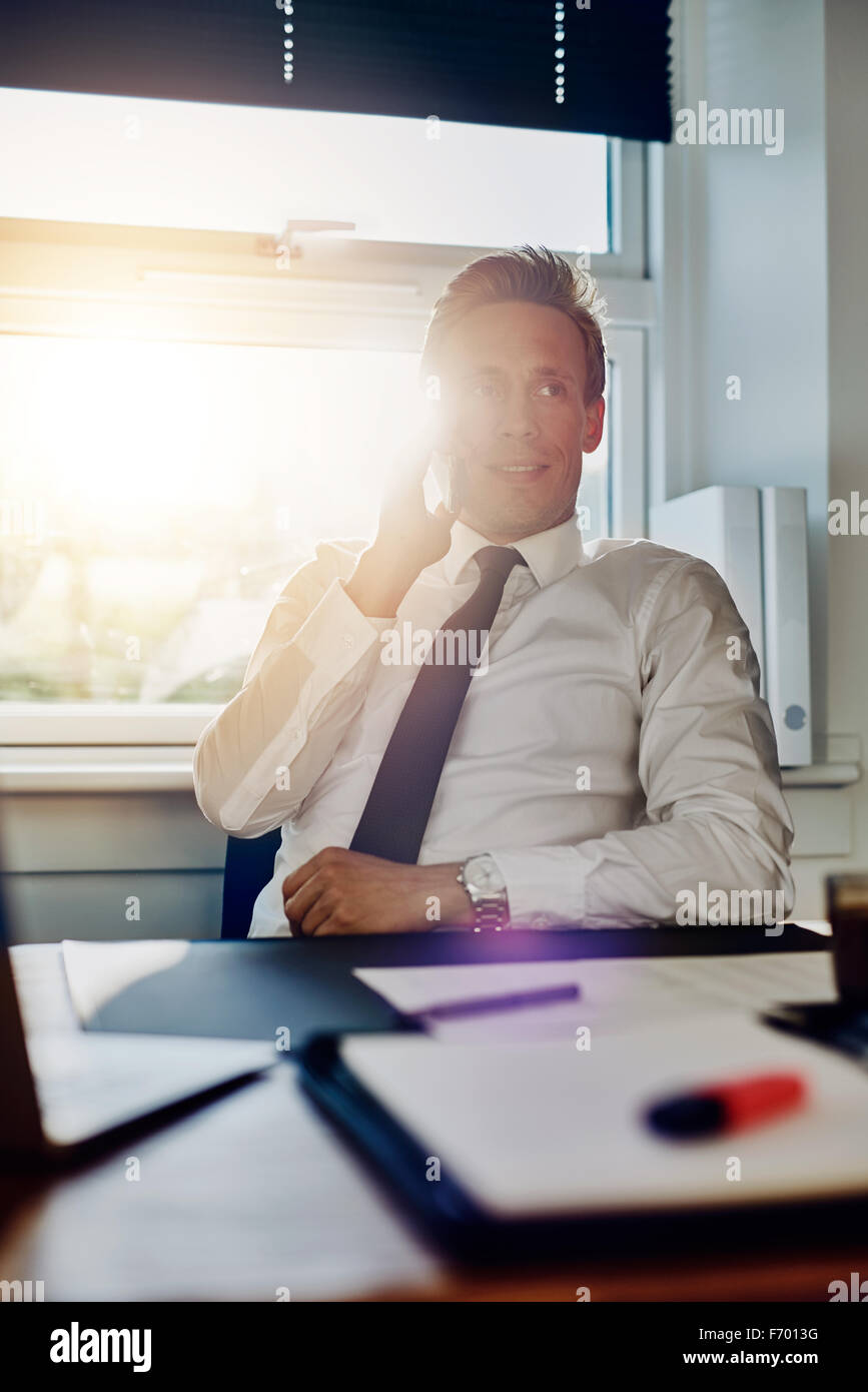 Business man speaking on the phone while sitting at his desk with ...