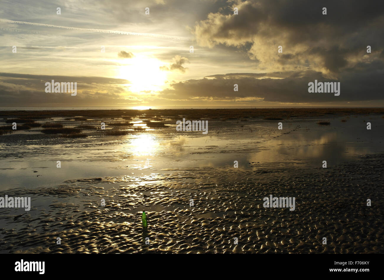 Sand ripples beach with glass bottle towards saltmarsh and yellow sun ...