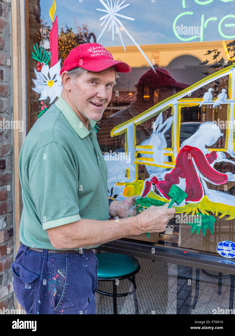 A Christmas window painter stands outside of a store window he is in ...