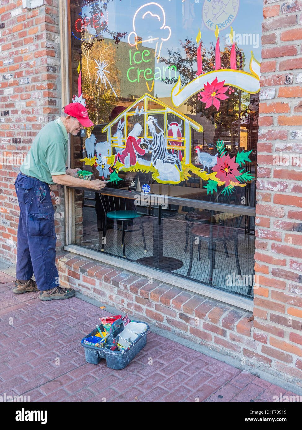 A Christmas window painter stands outside of a store window he is in ...