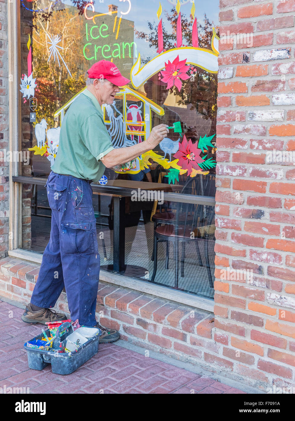 A Christmas window painter stands outside of a store window he is in ...