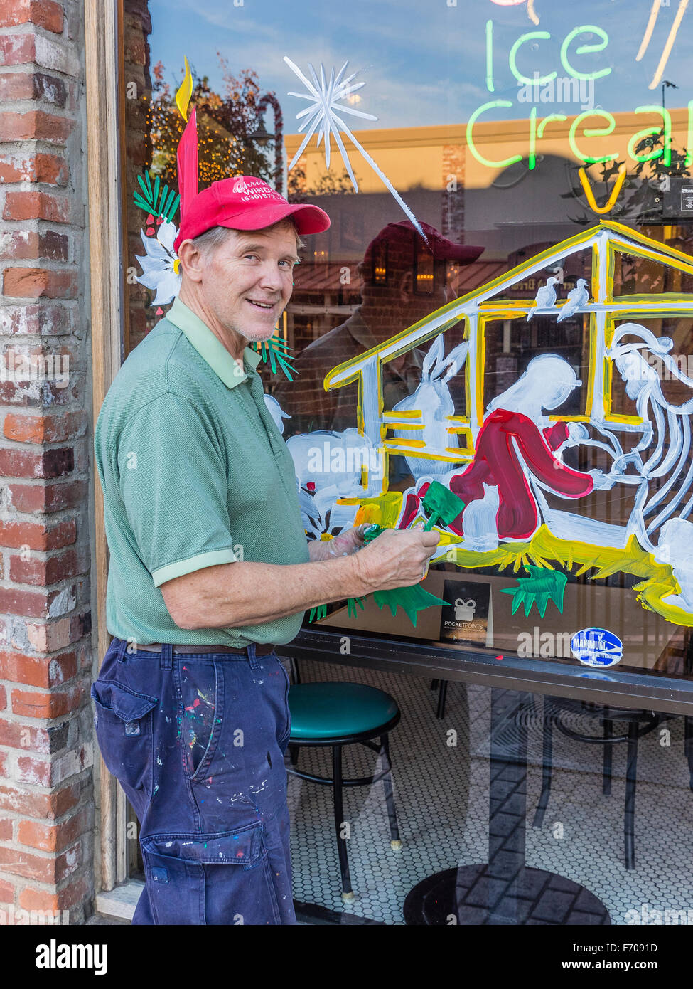A Christmas window painter stands outside of a store window he is in ...