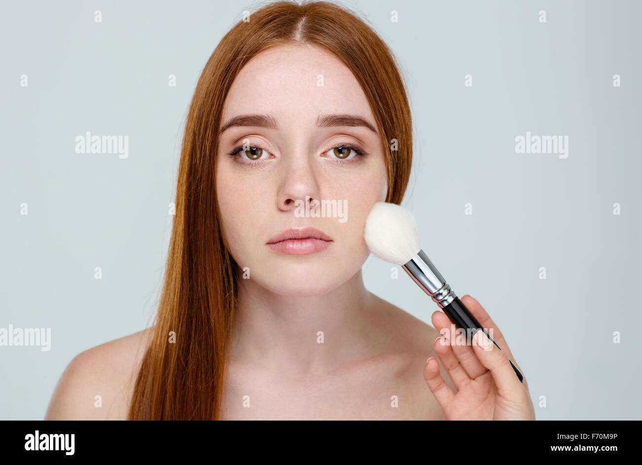 Portrait of a young redhair woman using makeup brush isolated on a ...