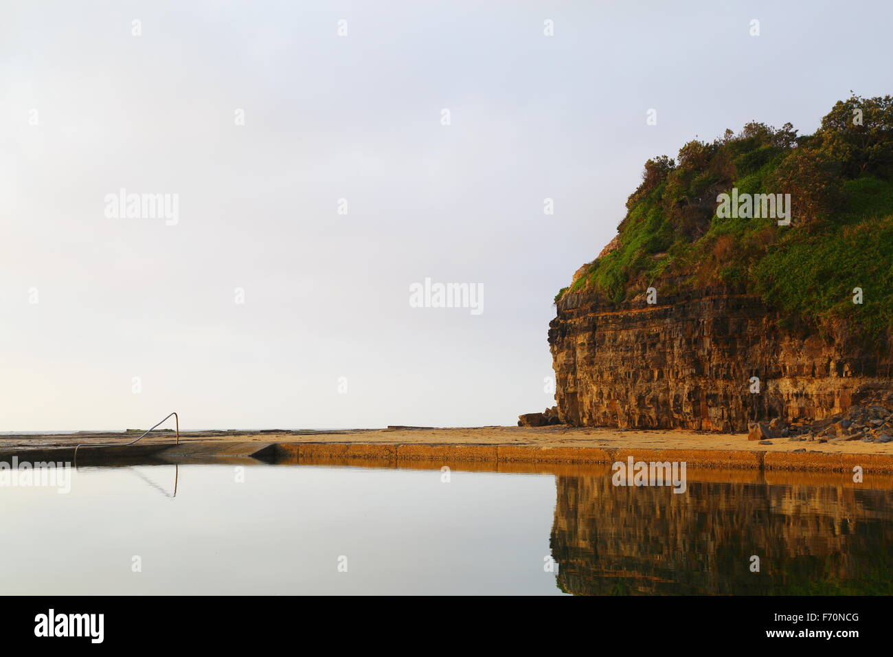 A headland bluff rises over the Wombarra Rock Pool - an ocean-water ...