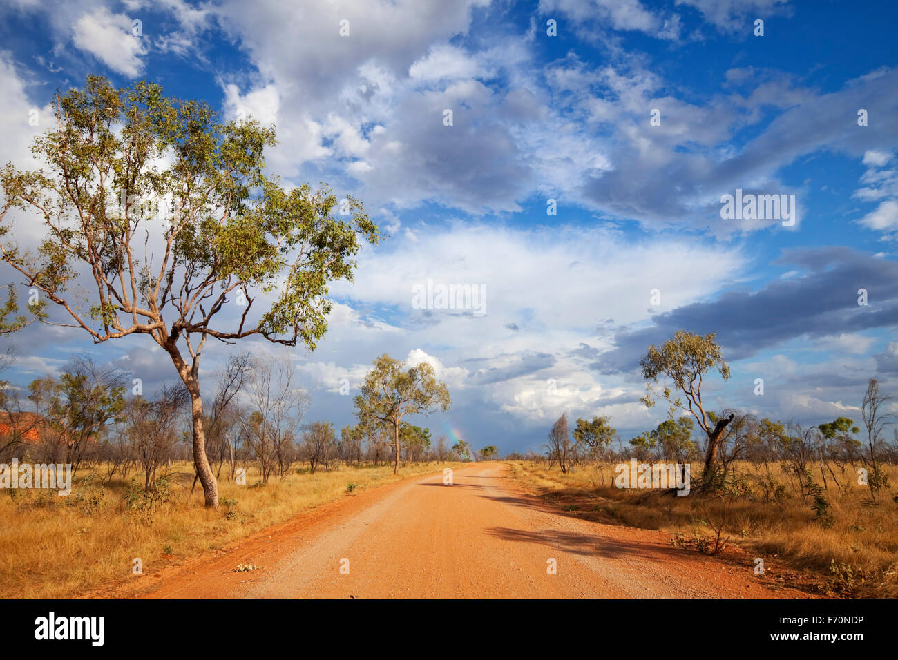 An unsealed road through the Australian outback with a rainbow at the ...