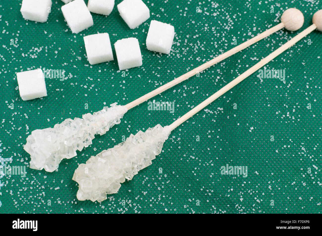 Two sugar sticks and sugar cubes on green with sugar grains spread ...