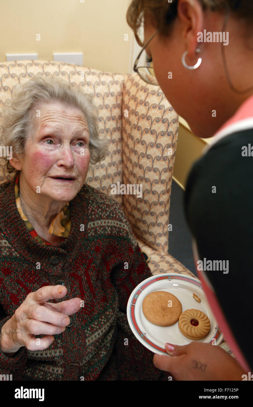 Care assistant offering a plate of biscuit to an older woman Stock ...