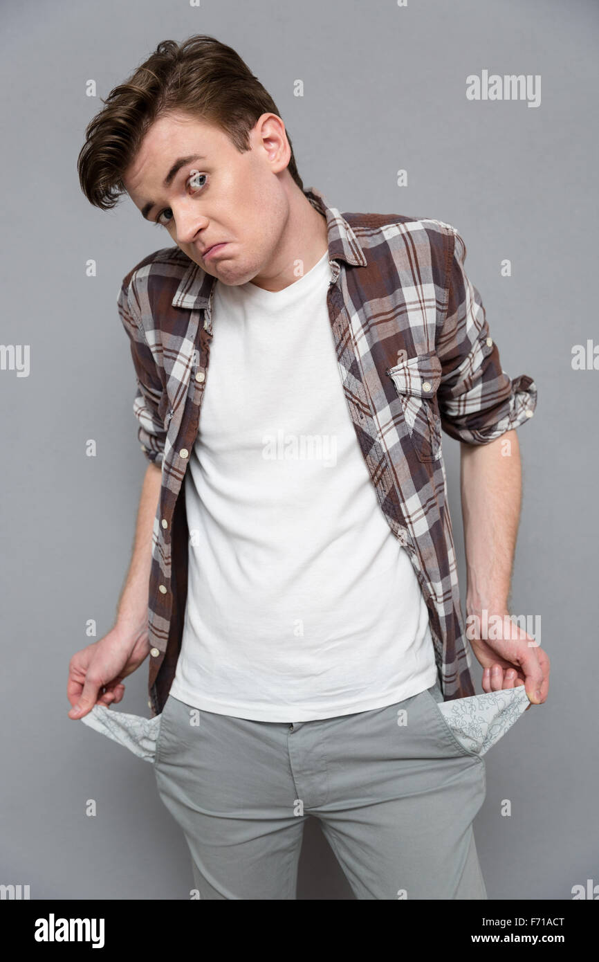 Portrait of a sad man exhibiting his empty pockets on gray bakground ...