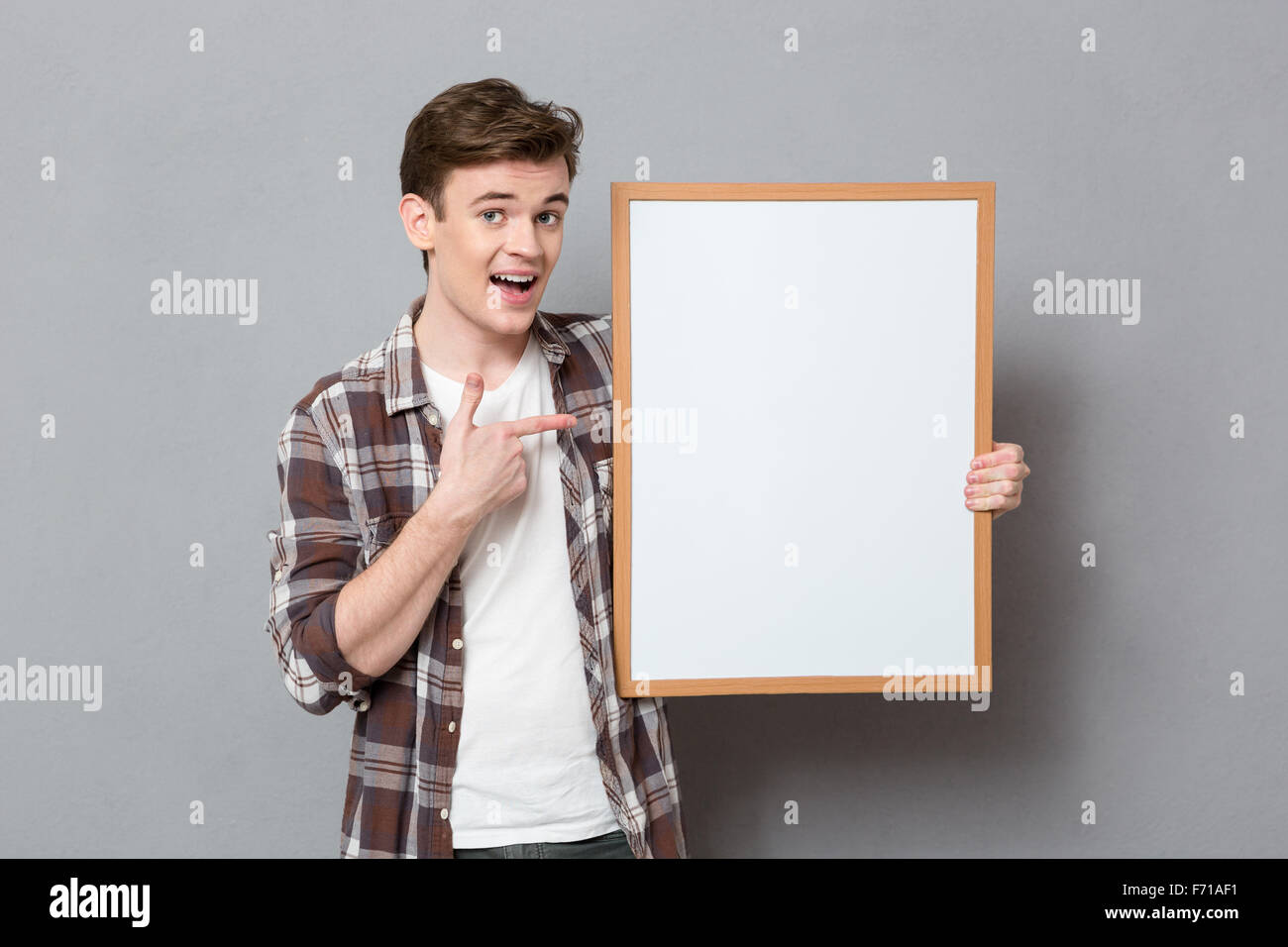 Portrait of a young man pointing finger on blank board over gray ...