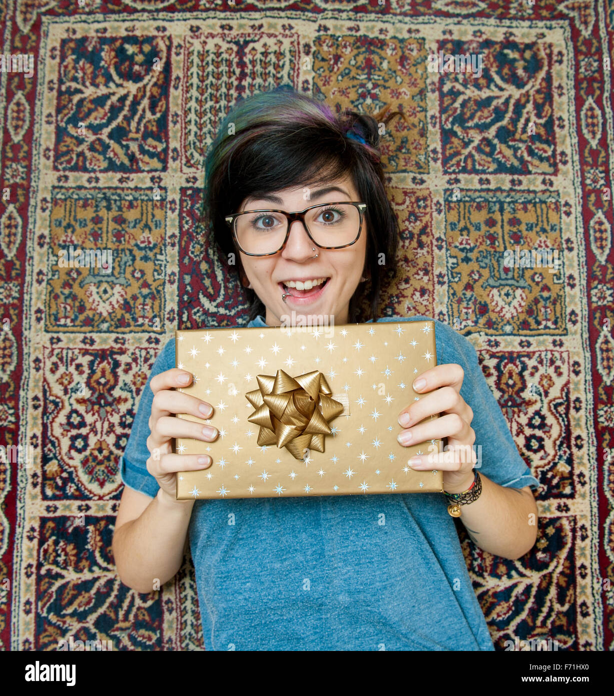 Pretty young woman cheerful holding gold gift pack between her hands ...