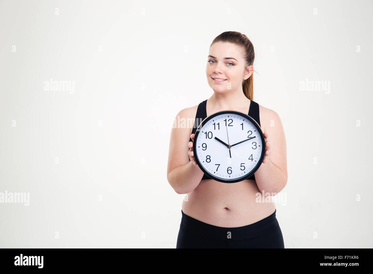 Portrait of a happy fat woman holding clock isolated on a white ...