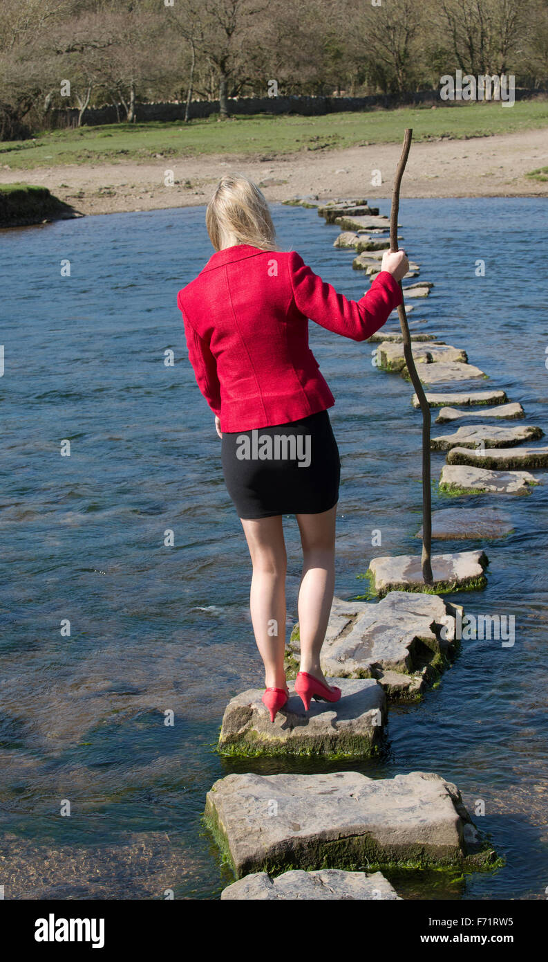 Woman holding a stick to test depth of water crossing a river using ...