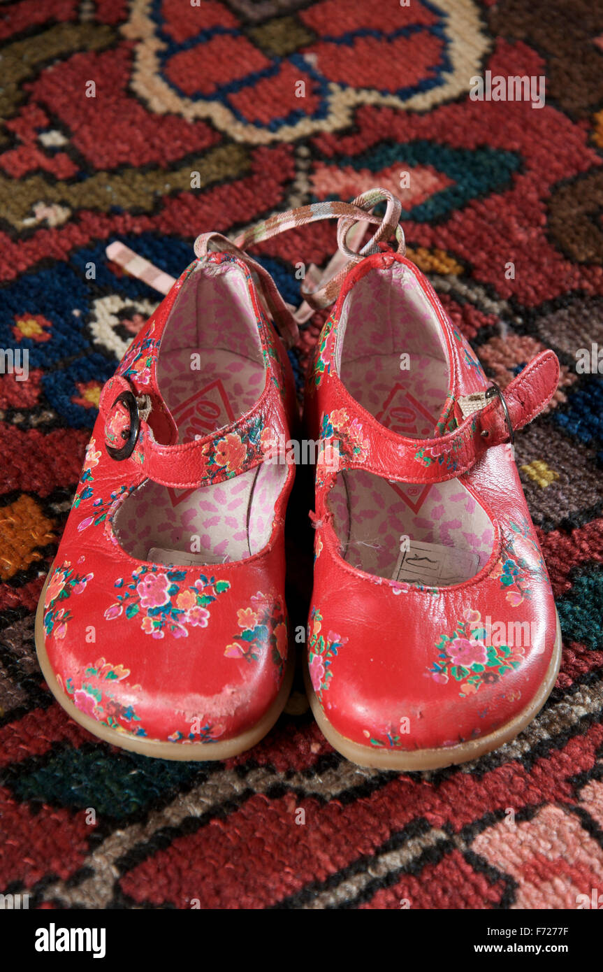 A well worn pair of little girl’s bright red leather shoes placed on a ...