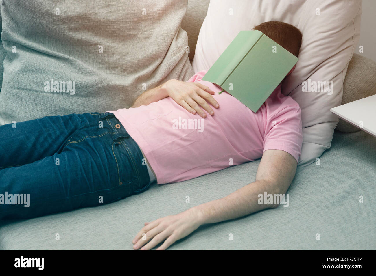 man in jeans and tshirt sleeping on couch with book on his head Stock ...