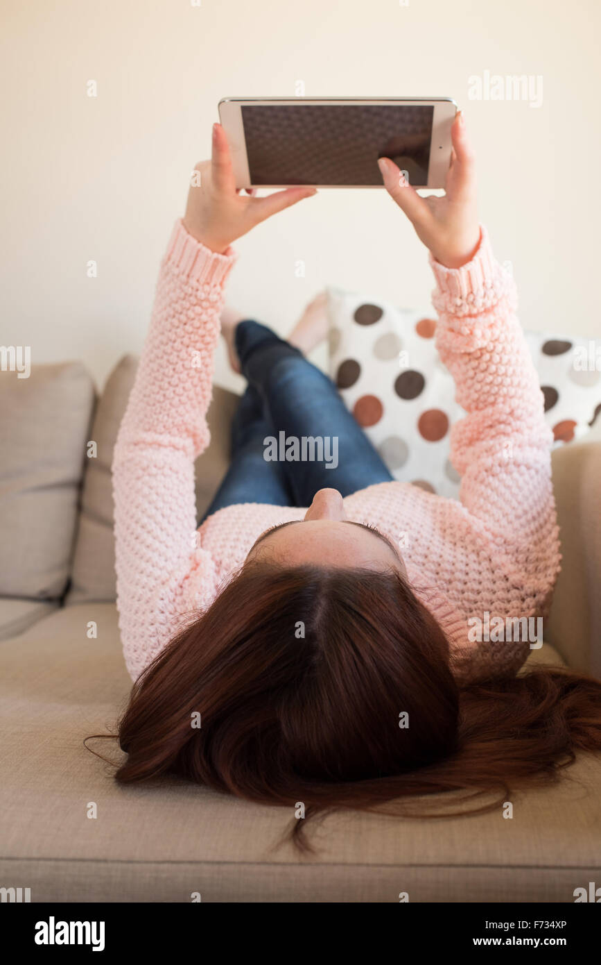 Woman lying down on couch with a tablet Stock Photo - Alamy
