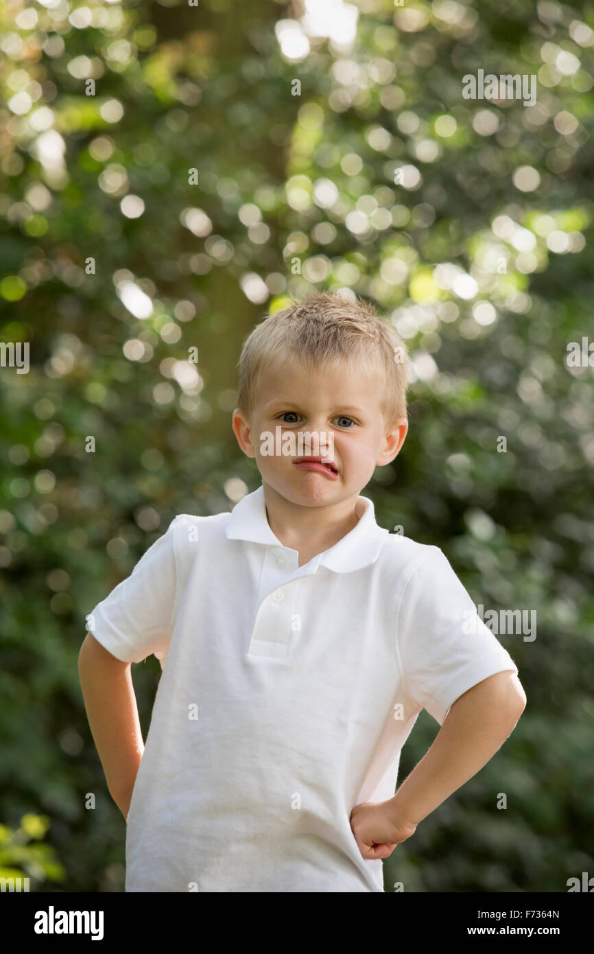 Young boy standing in a forest, looking at the camera, pulling a face ...