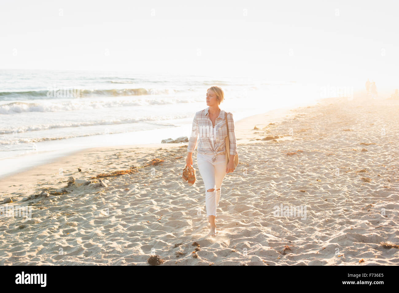 Woman walking along a sandy beach by the ocean Stock Photo - Alamy